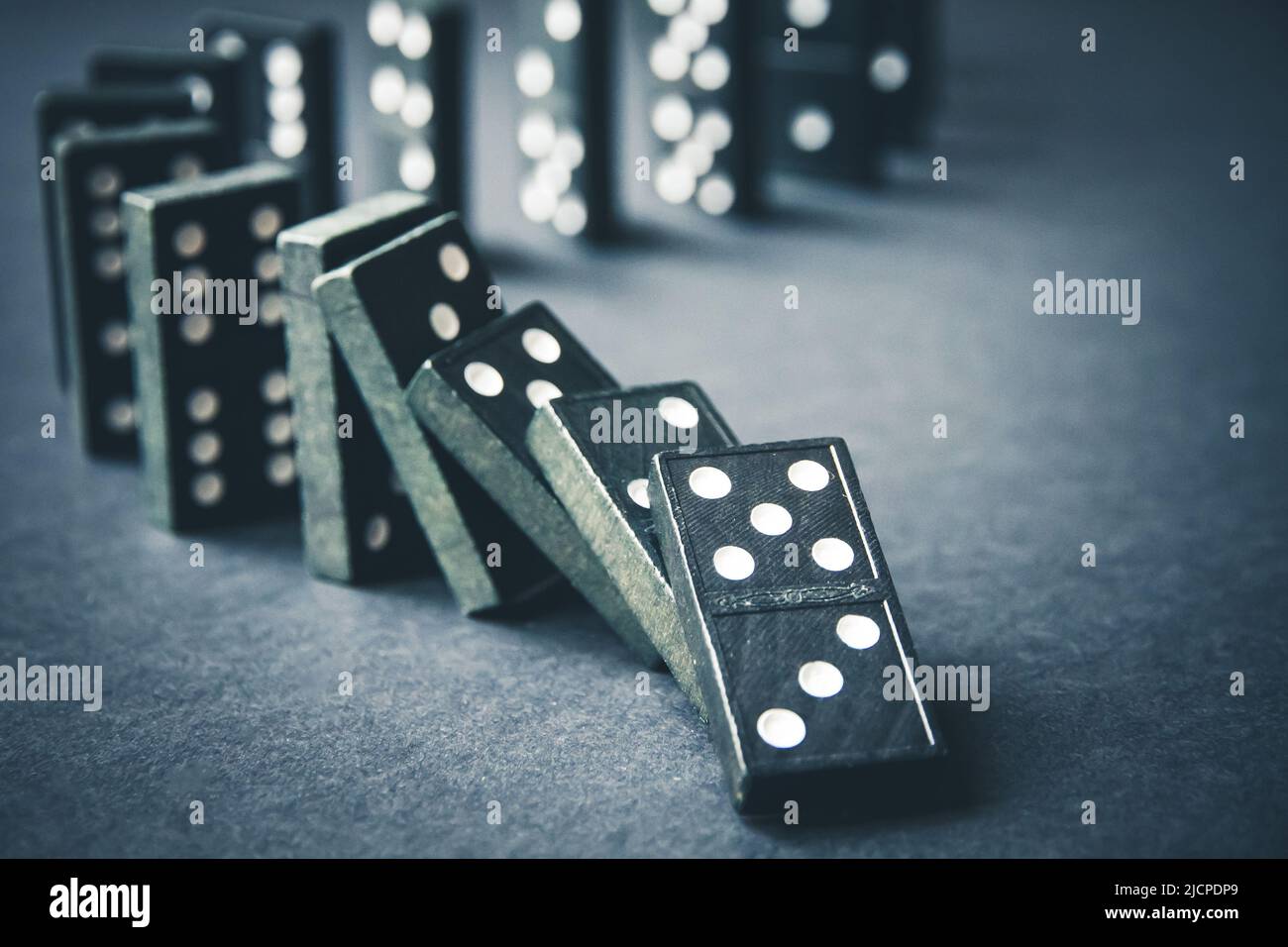 Black dominoes chain on a dark table background. Domino effect concept ...