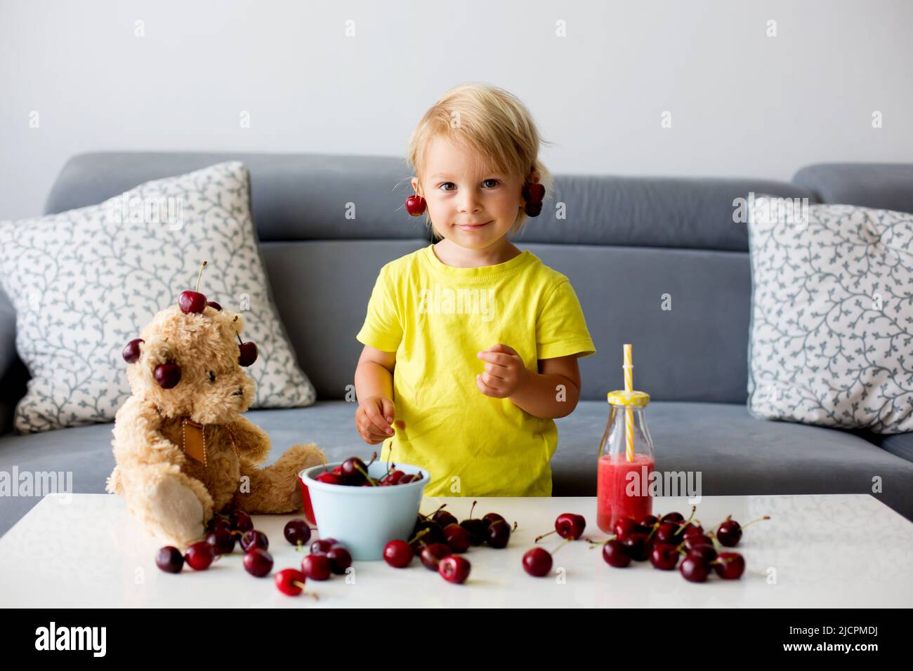 Toddler blond child, cute boy, eating cherries with teddy bears at home ...