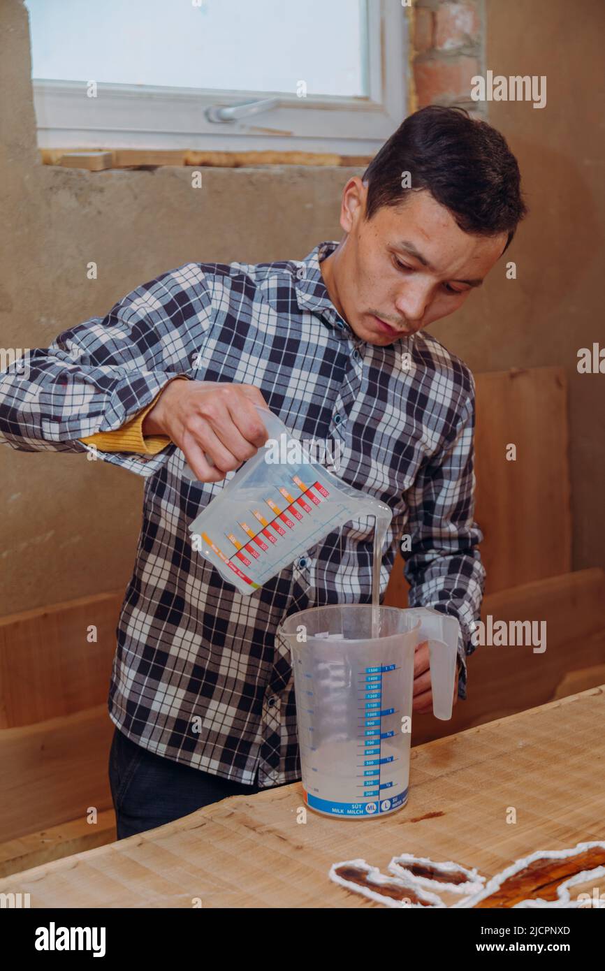Carpenter pouring epoxy resin into liquid cup. Process of making a ...