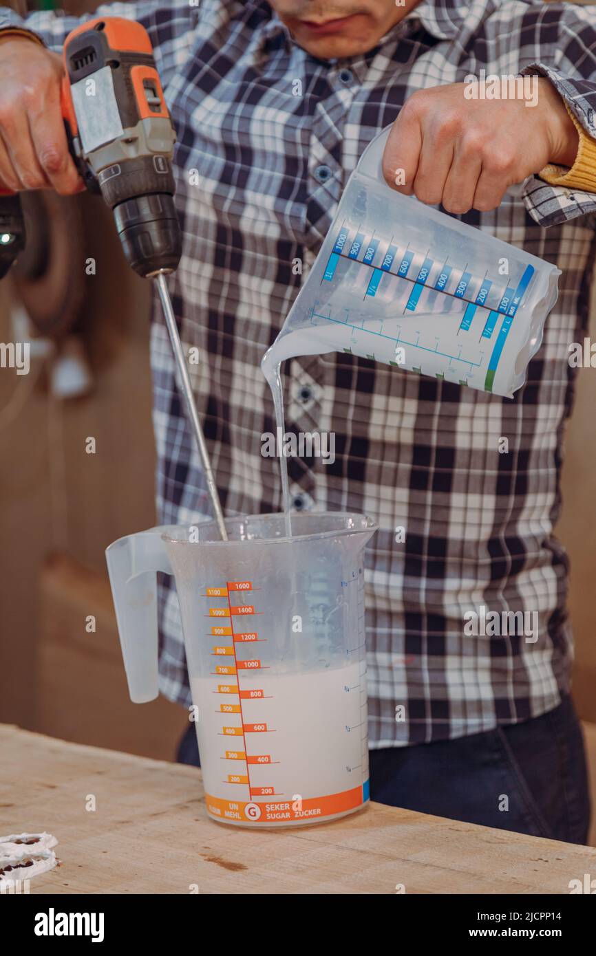 Carpenter mixing epoxy resin with an electric mixer in liquid cup in ...