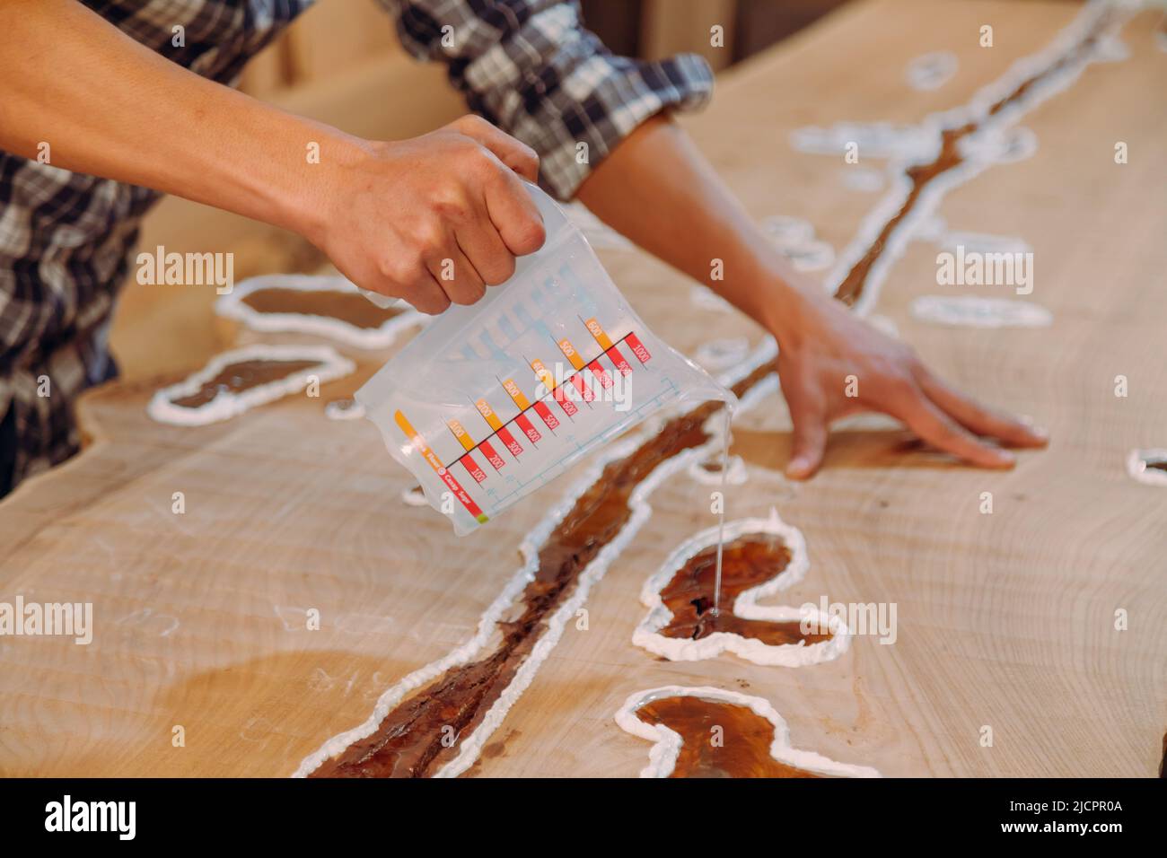 Carpenter pouring epoxy liquid in a wooden table. Process of making a ...