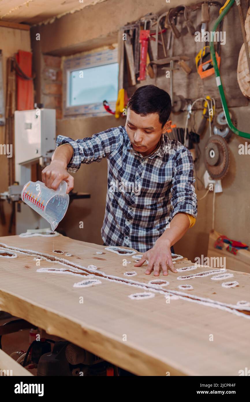 Carpenter pouring epoxy liquid in a wooden table. Process of making a ...