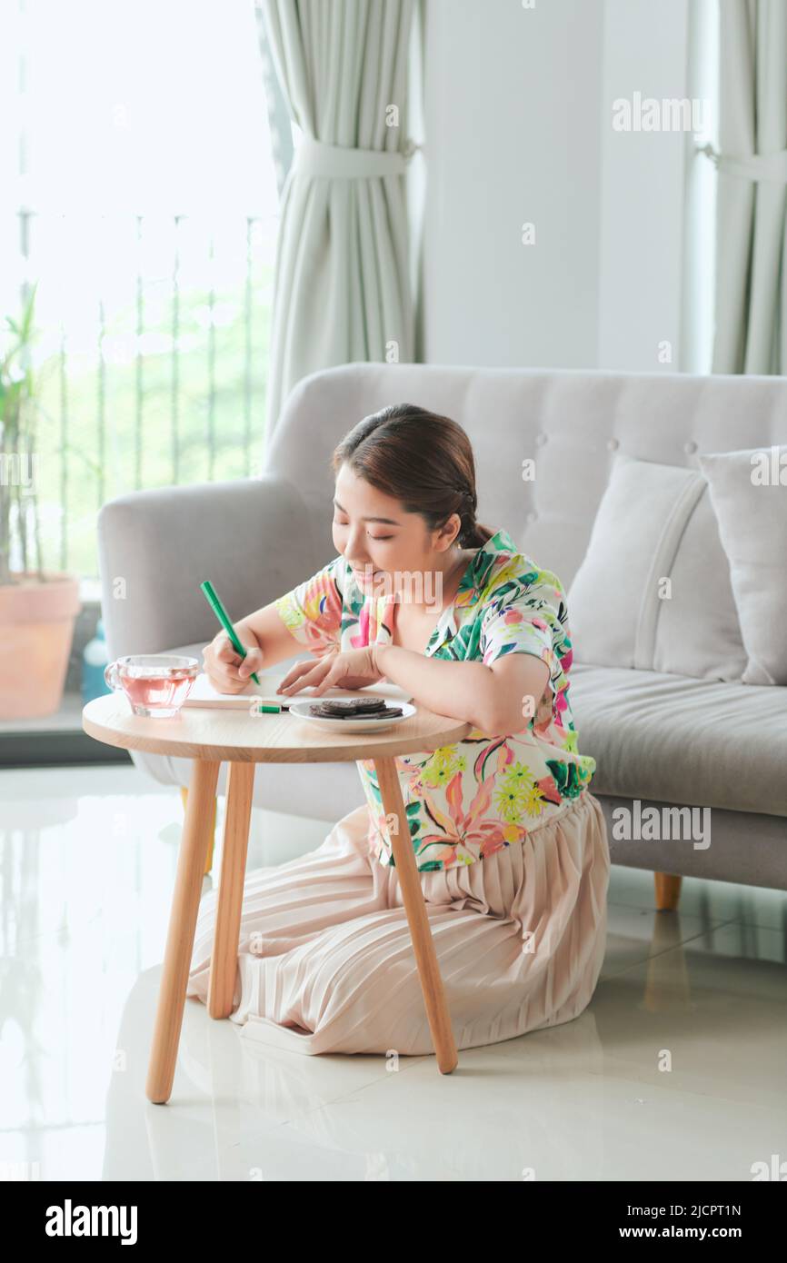 Pretty woman writing near couch at home in the living room Stock Photo ...