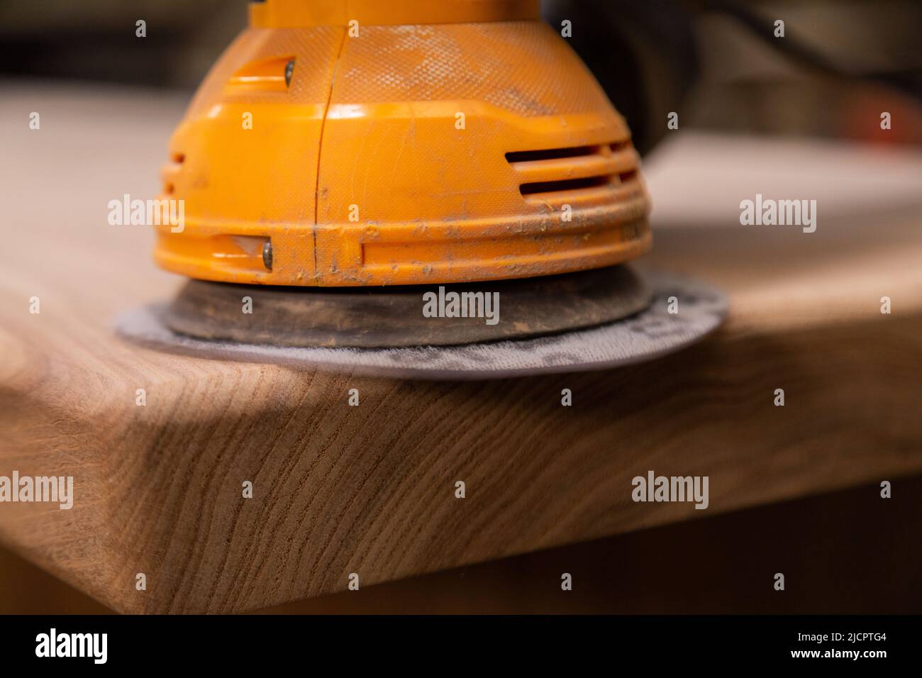 Closeup of carpenter sanding wood table with orbital sander in a ...