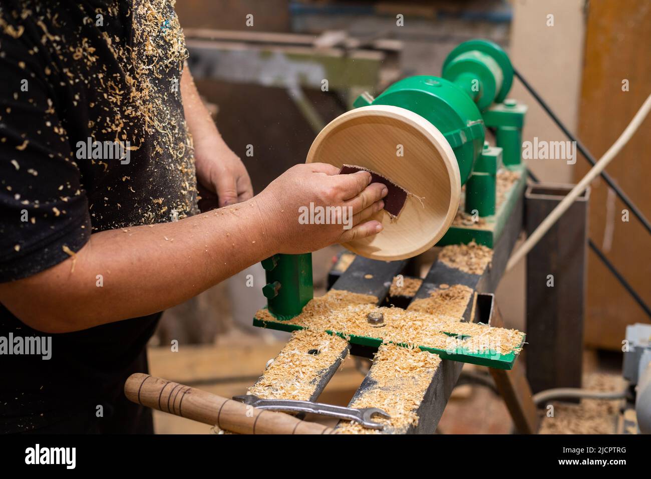Closeup of person sanding wooden product using sandpaper on a lathe ...