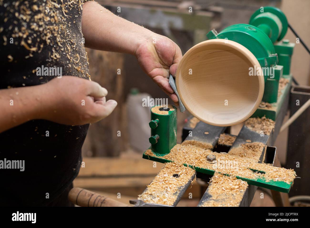 Closeup of person sanding wooden product using sandpaper on a lathe ...