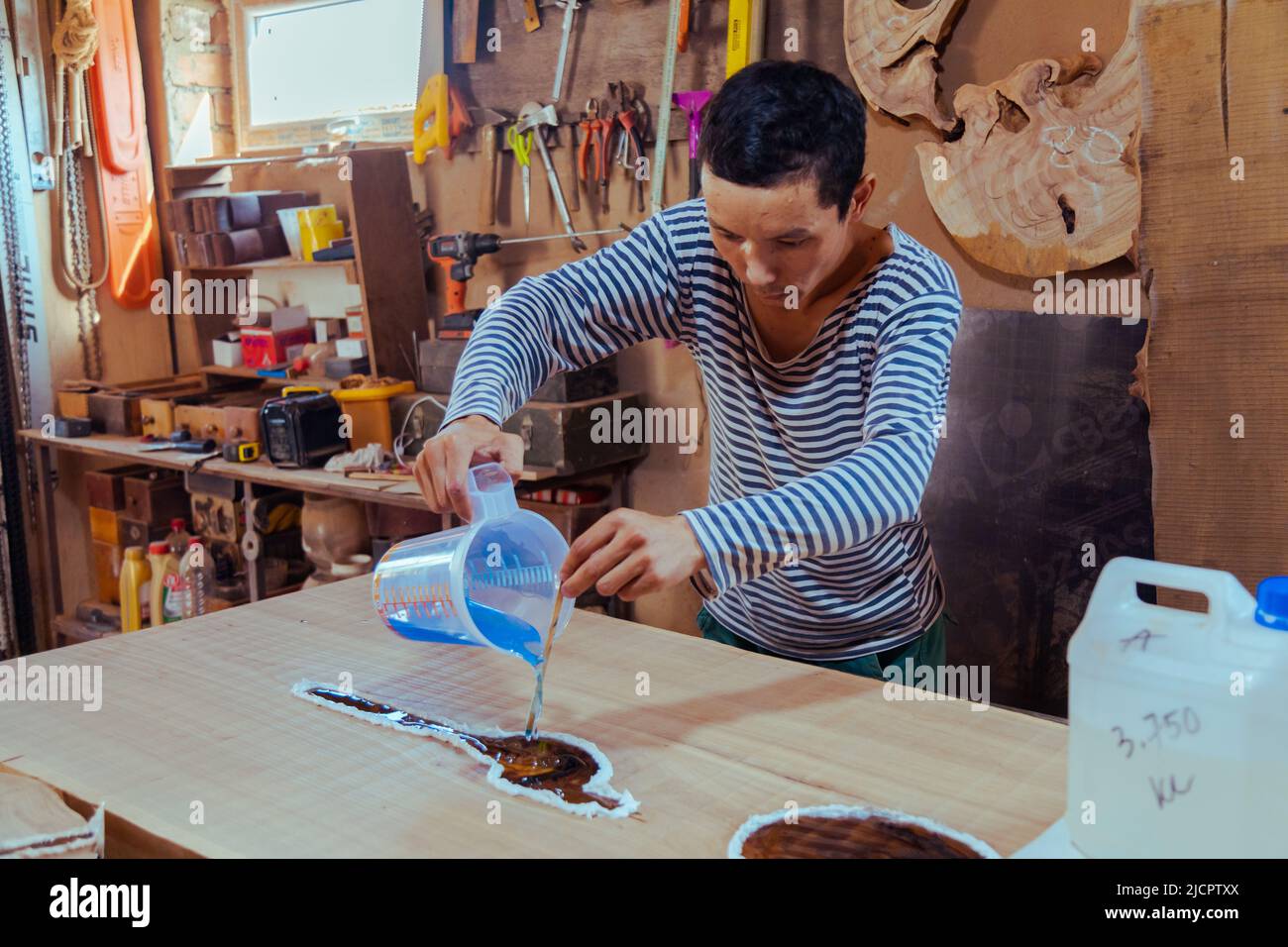Carpenter pouring liquid epoxy in a wooden table. Process of making a ...