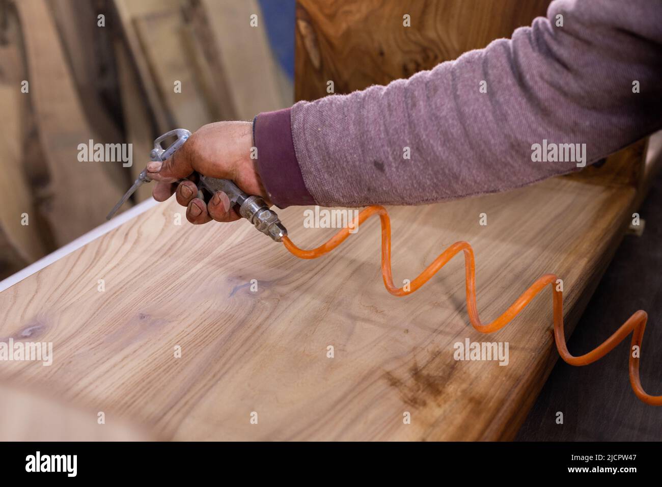 Man blowing dust off the surface of wooden table in the workshop ...