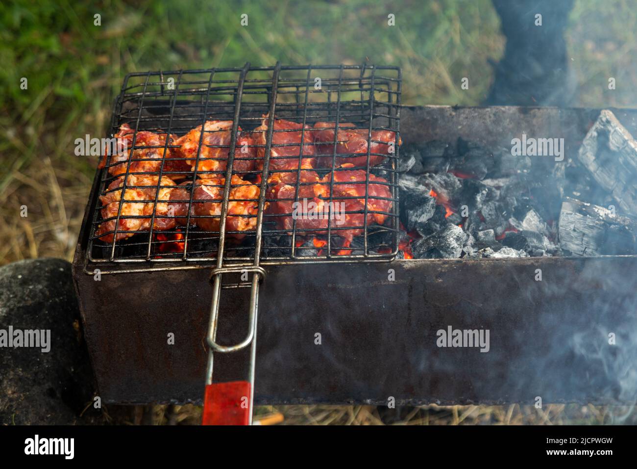 Grill grate with red meat on a brazier with flaming charcoal. Outdoor ...