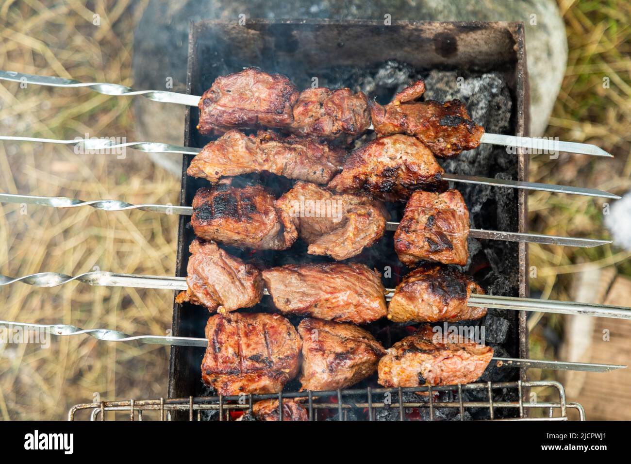 Top down view beef meat on steel skewers grilling on brazier with ...