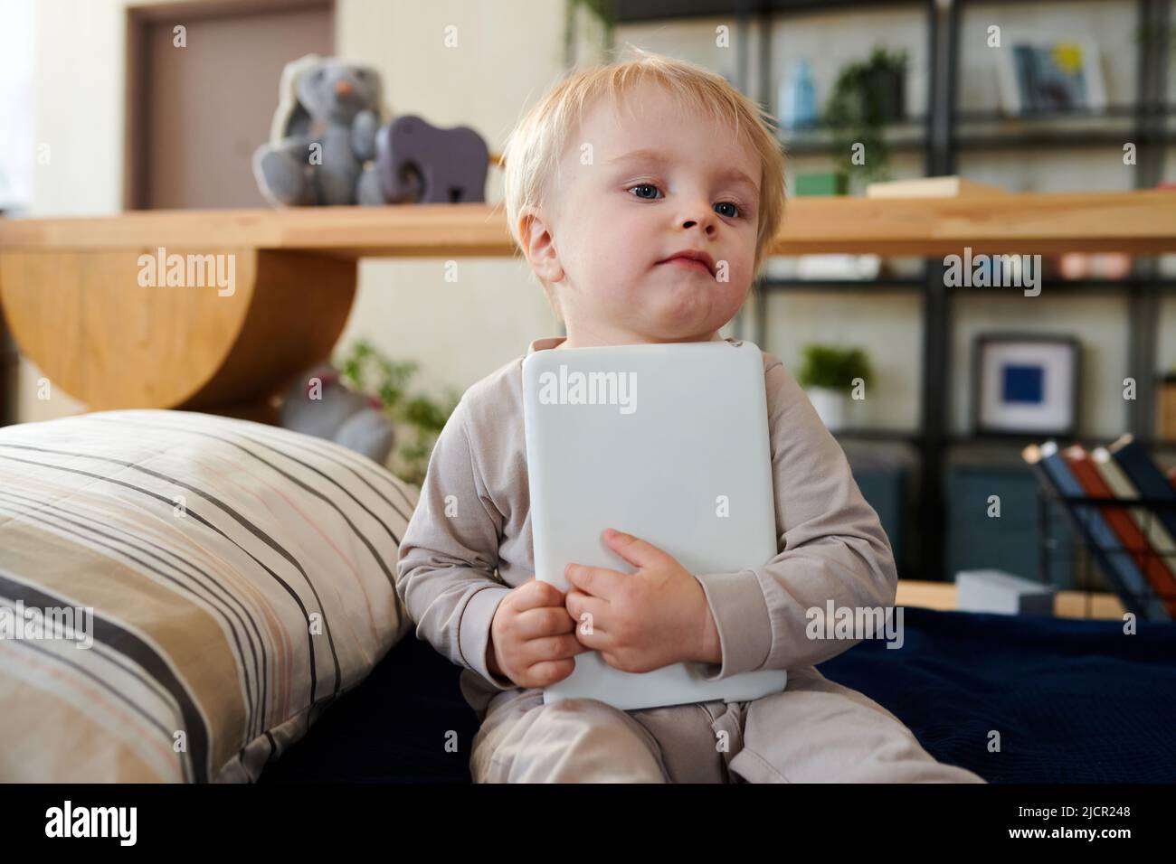 Cute little child sitting on bed with digital tablet and playng with it ...