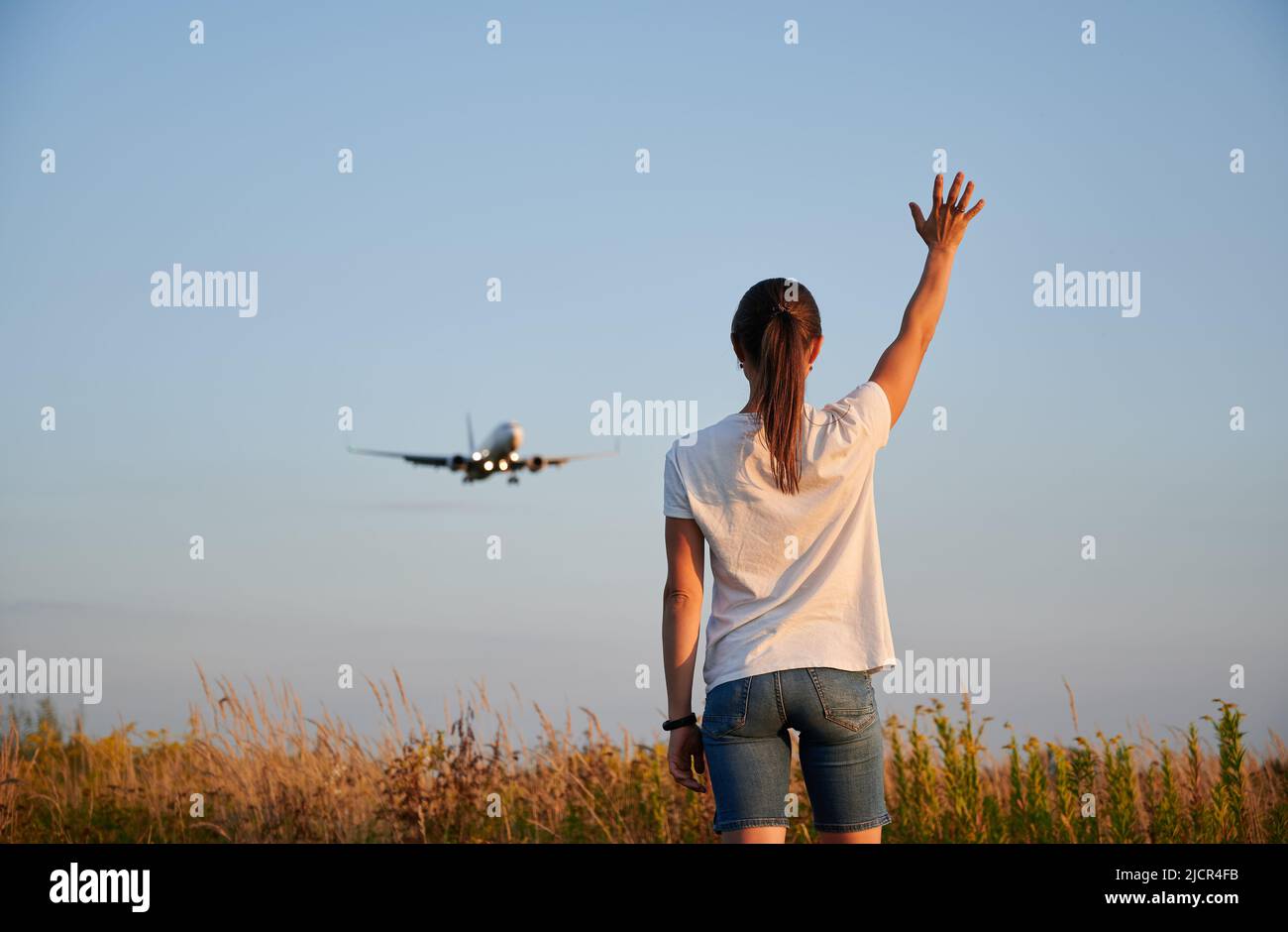 Back view of woman waving hand to flying commercial airplane in the sky ...