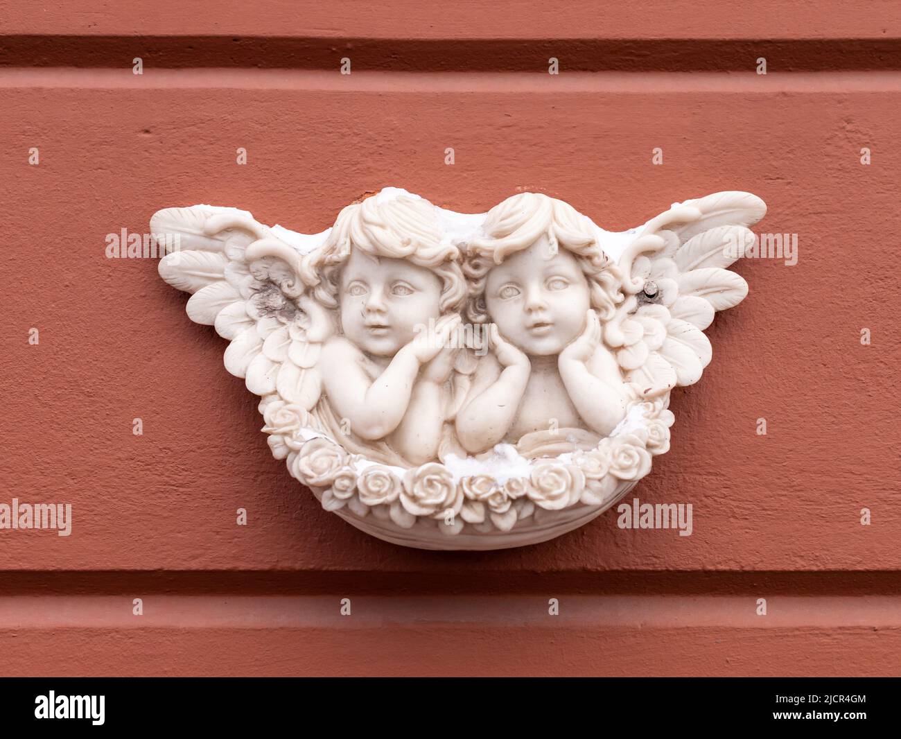 Two baby angels with wings marble sculpture on red wall of building ...