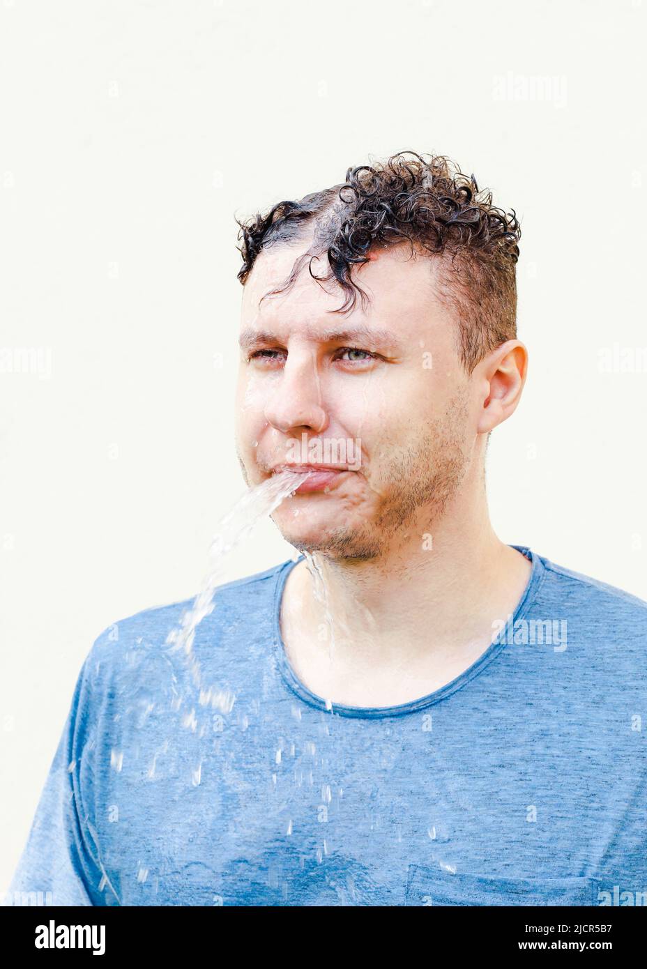 Wet young caucasian man in blue t-shirt with curly hair is spitting ...