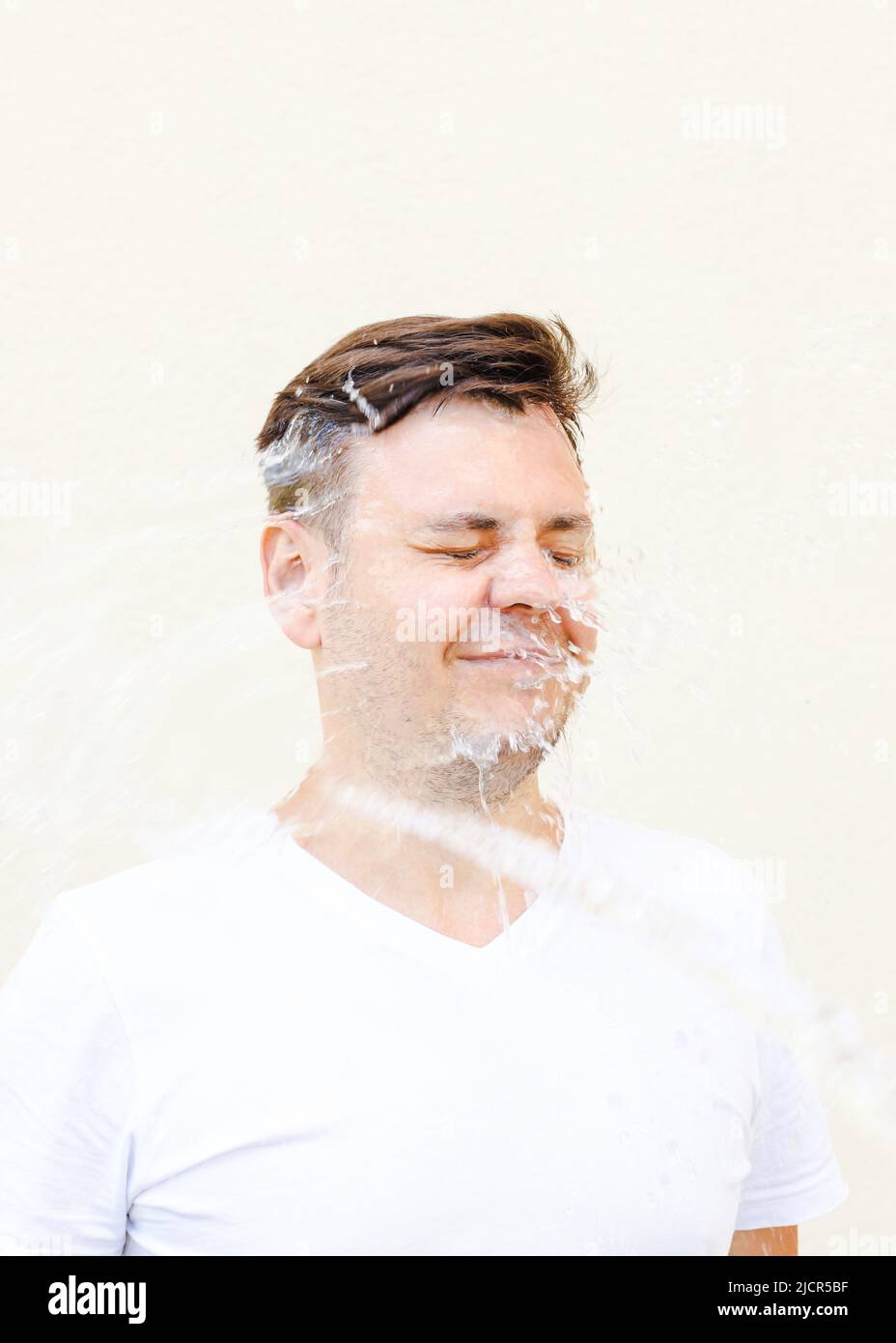 Wet young caucasian man in white t-shirt with closed eyes in water ...
