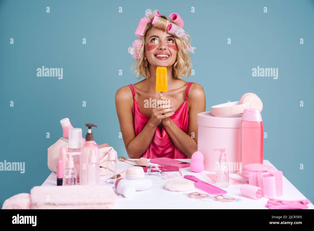 Young woman eating ice cream by table with beauty products isolated ...