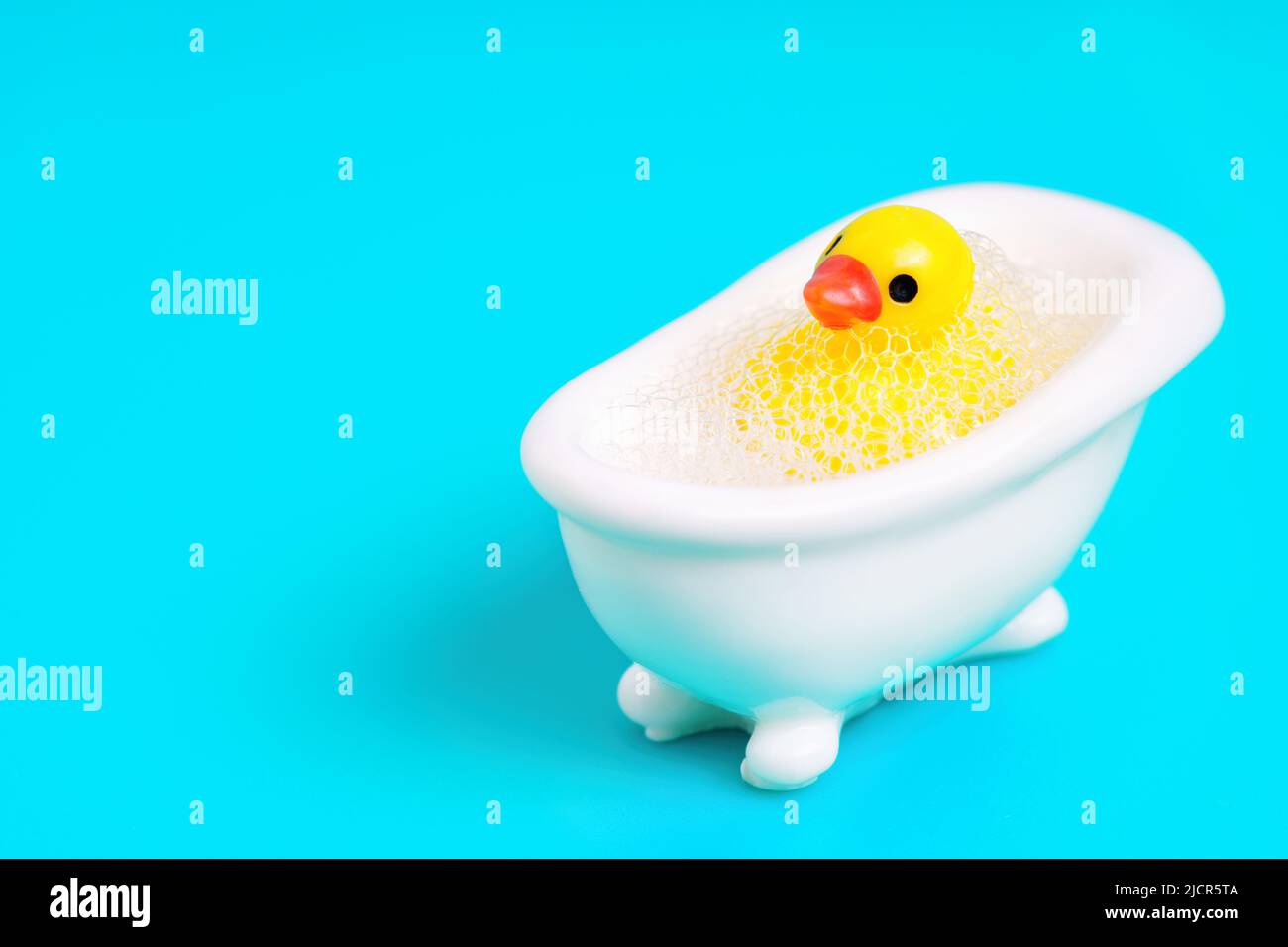 Toy yellow duck taking a soapy bath on blue background. Developing ...