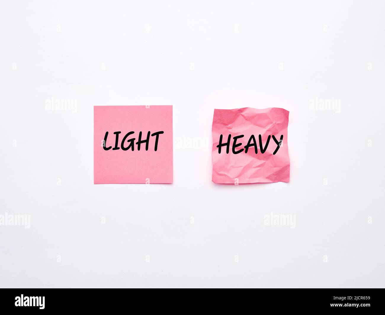 The words heavy and light on pink sheets of note paper Stock Photo - Alamy