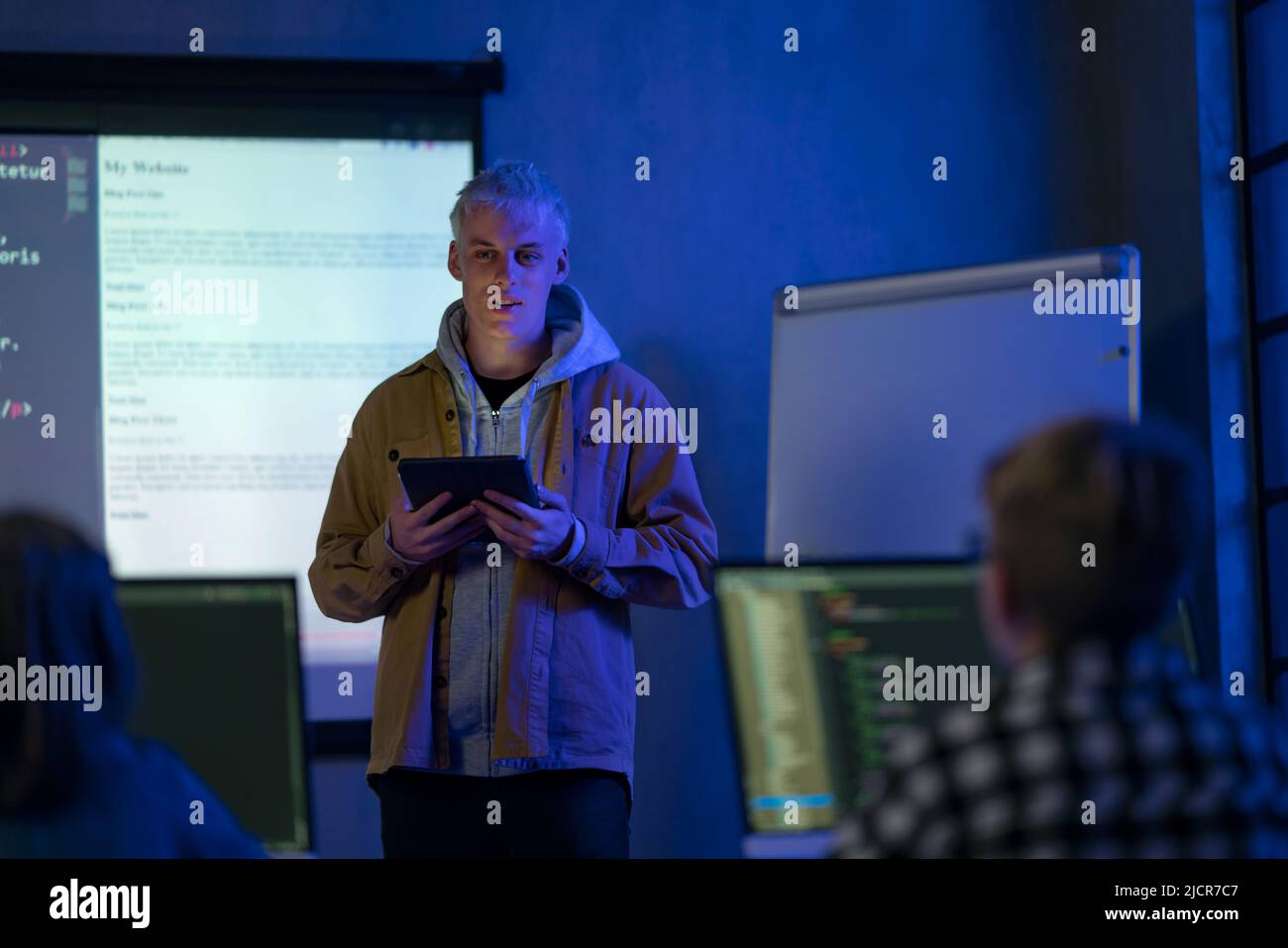 Teacher giving computer science lecture to young students in dark room ...