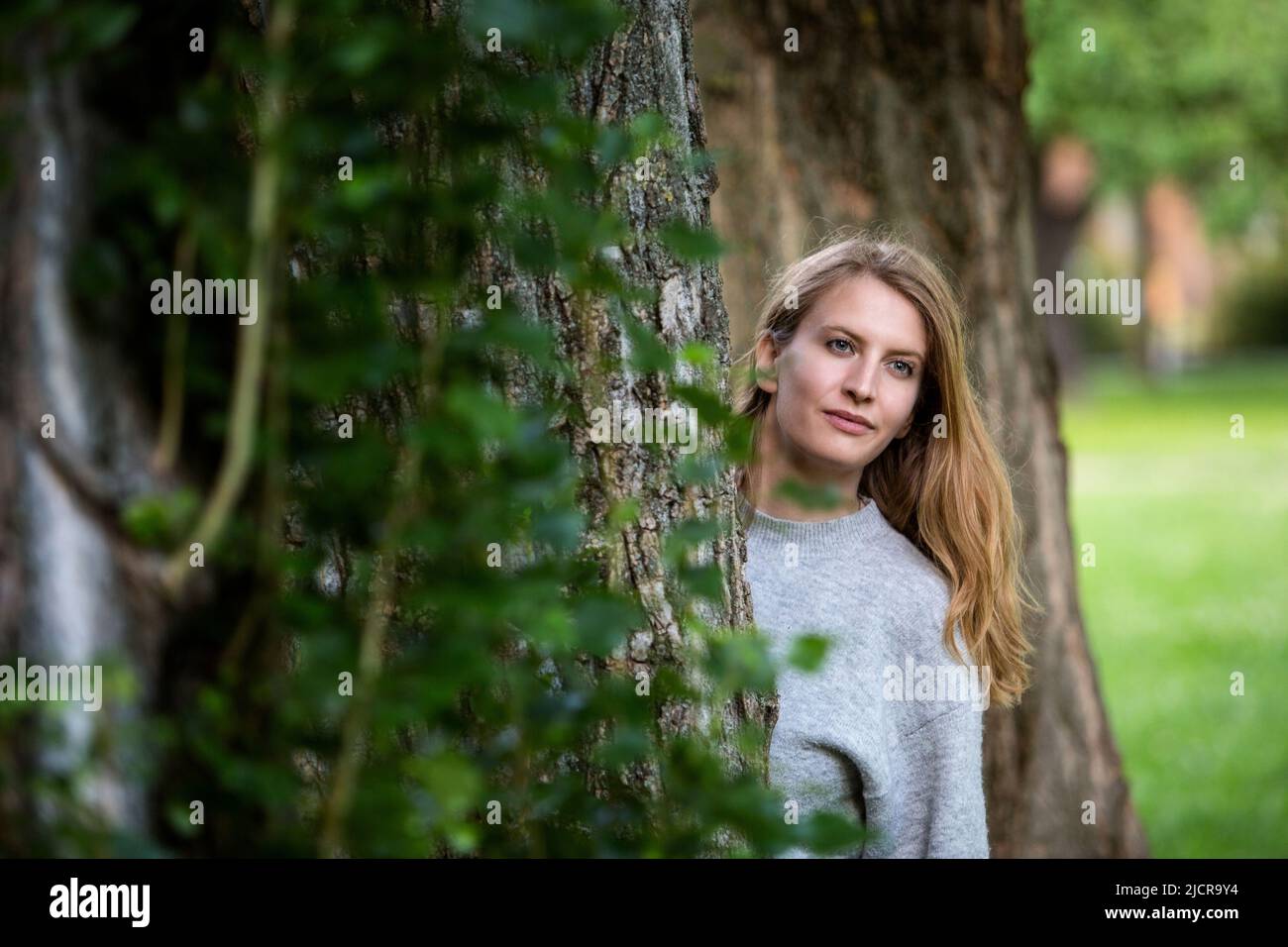 portrait of blond woman standing between trees Stock Photo - Alamy