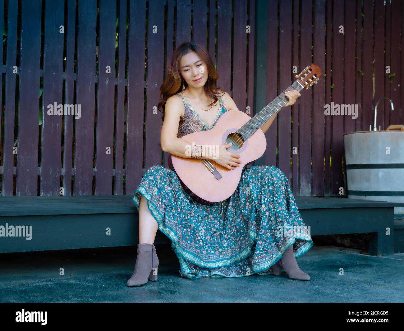 A beautiful woman sitting happily playing the guitar Stock Photo - Alamy