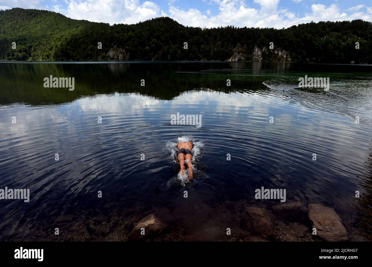 15 June 2022, Bavaria, Füssen: A man seeks to cool off by jumping into ...