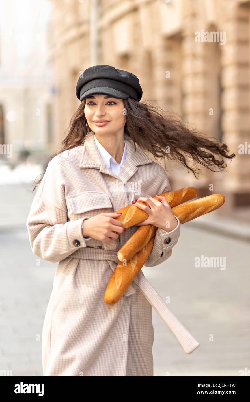 Portrait of a young woman in a spring coat and cap, with baguettes in ...