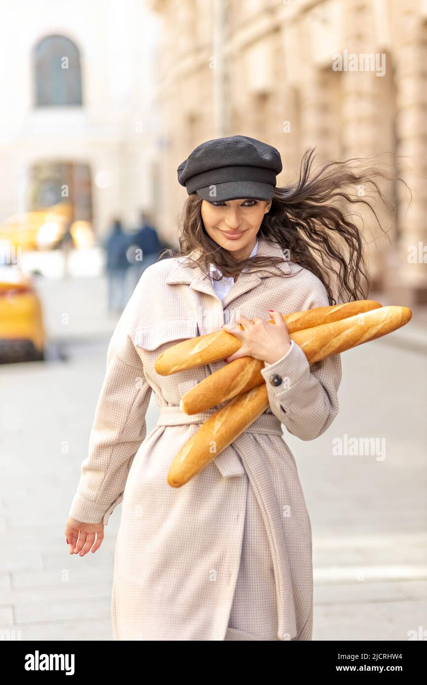 Portrait of a young woman in a spring coat and cap, with baguettes in ...
