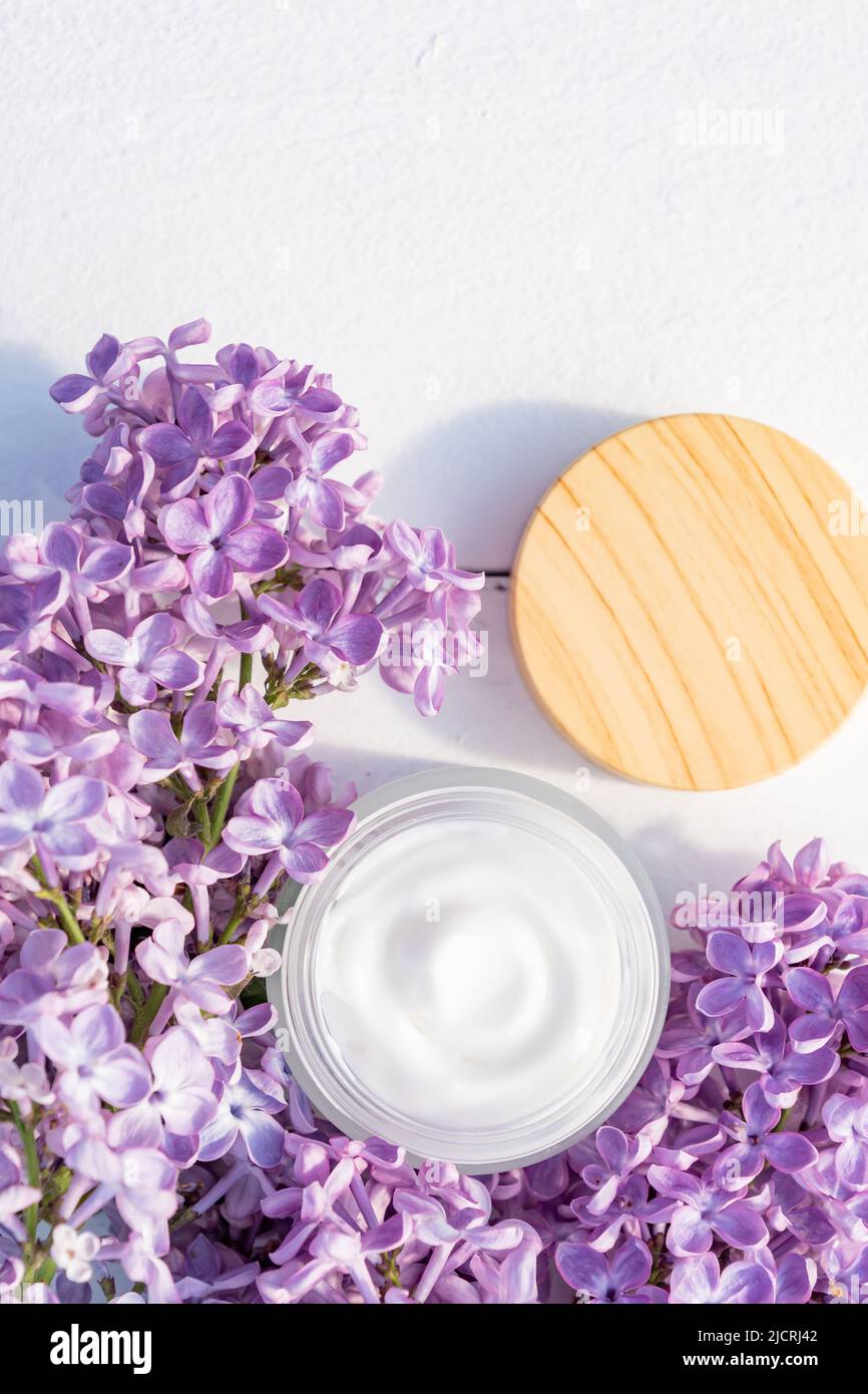 Jar of cream and lilac flowers on a white background, top view ...