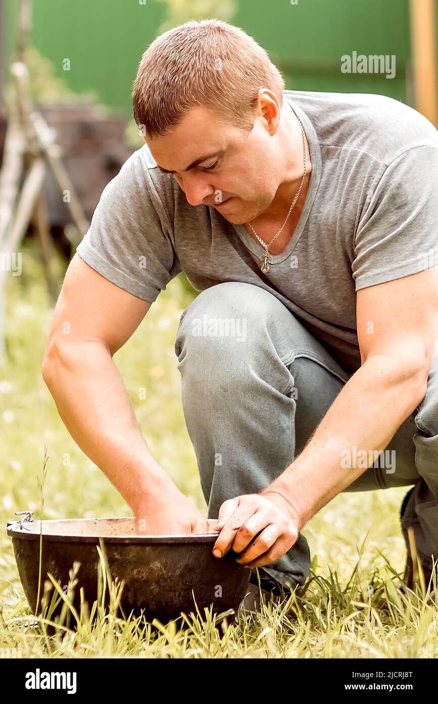 A man does his homework, cleans a cauldron in the backyard of a country ...
