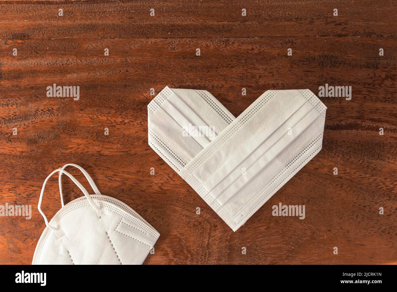 heart shape with white surgical masks on a rustic and natural wooden ...