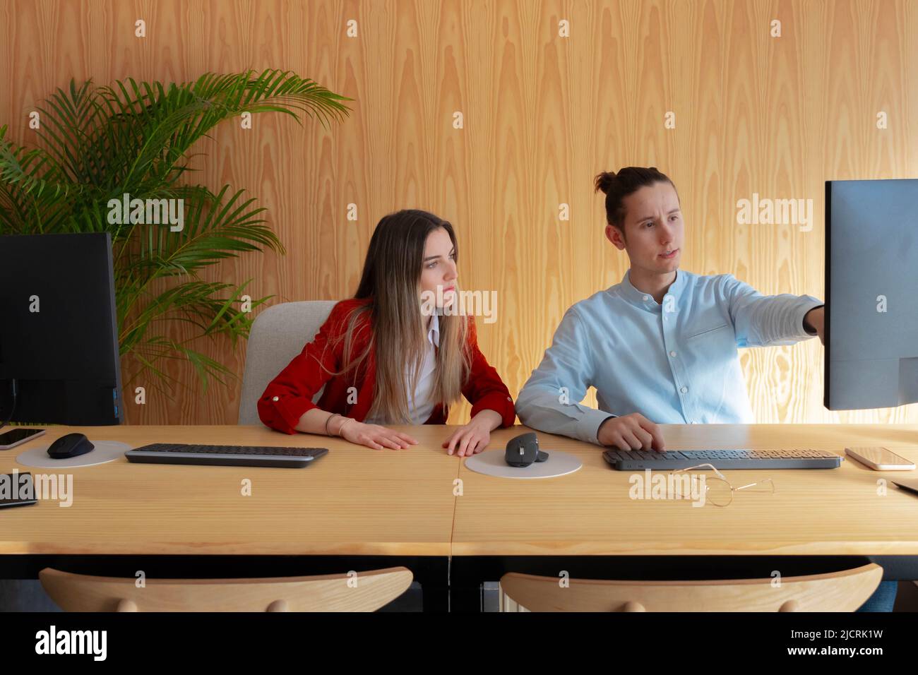 Two young workers working together in modern office with computers ...