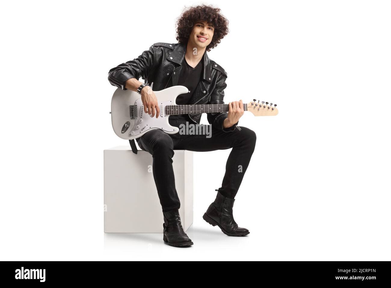 Young male rocker in a leather jacket sitting on a white cube with an ...