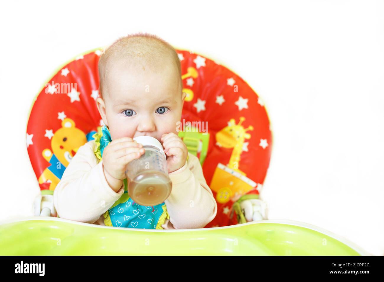 baby drinking from bottle sitting in the high chair on a white ...