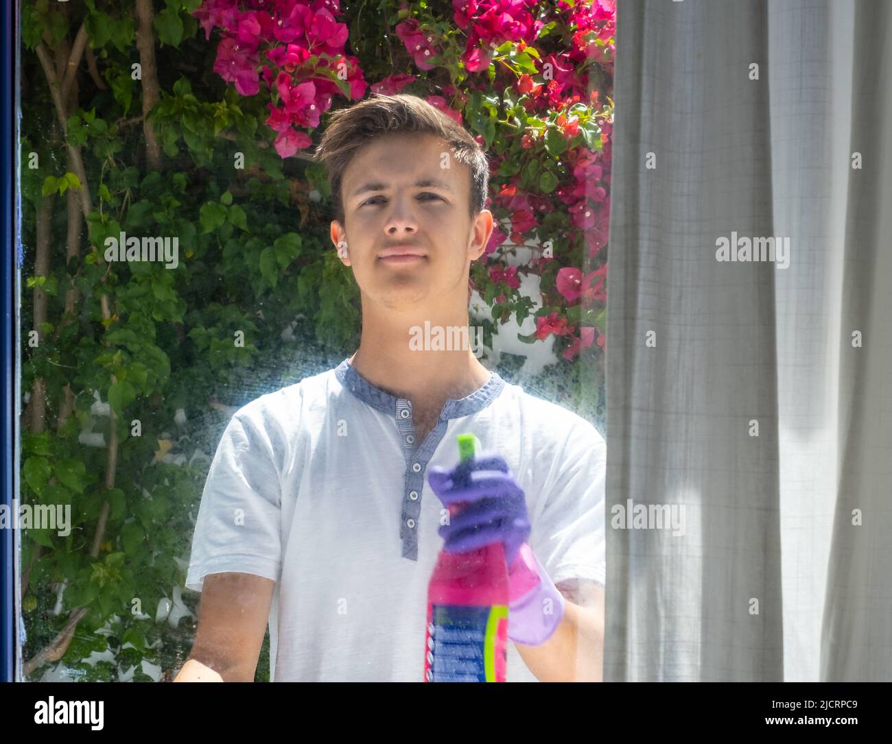 Handsome guy in gloves cleaning window with rag and detergent at home ...