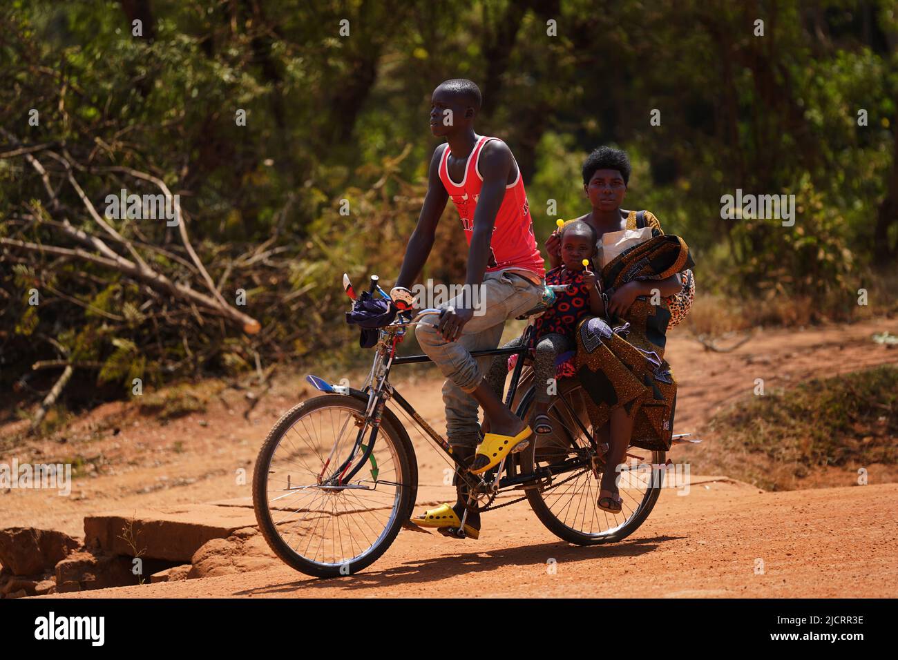 A family cycles along a street in countryside south of Kigali, Rwanda ...