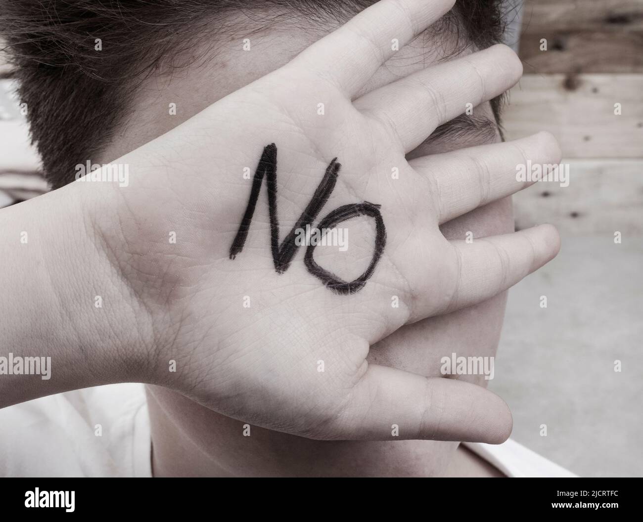 child covering his face with his hand with NO written on it in marker ...