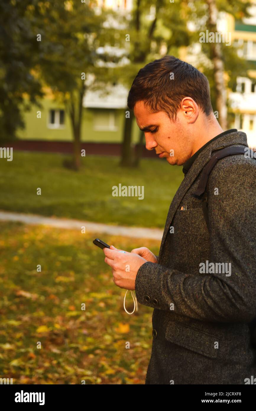 Defocus young man holding phone. Man using smart phone in autumn park ...