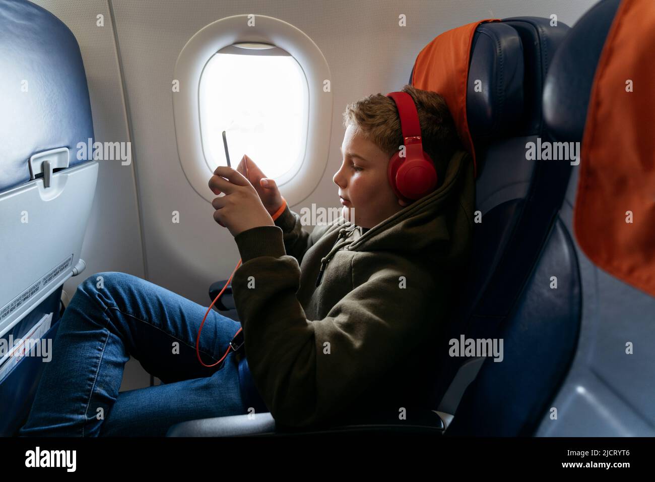 An boy is flying on a plane with headphones and playing on a tablet ...