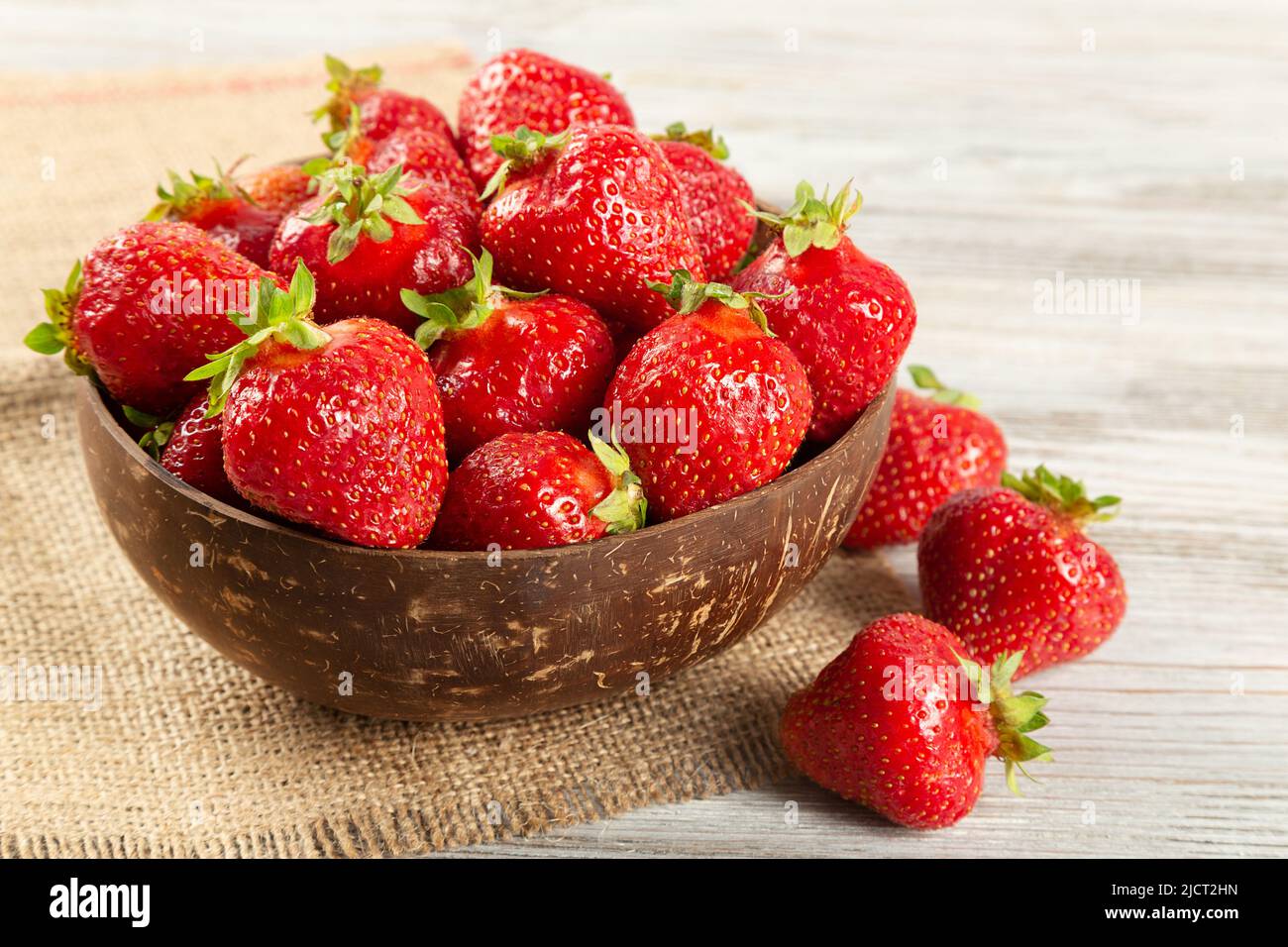 Fresh juicy ripe red strawberry in a brown coconut plate on a wooden ...