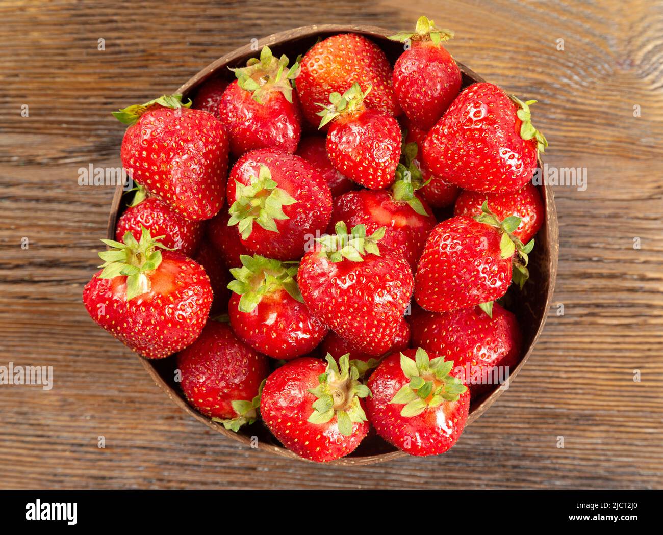 Fresh juicy ripe red strawberry in a coconut plate on a brown wooden ...