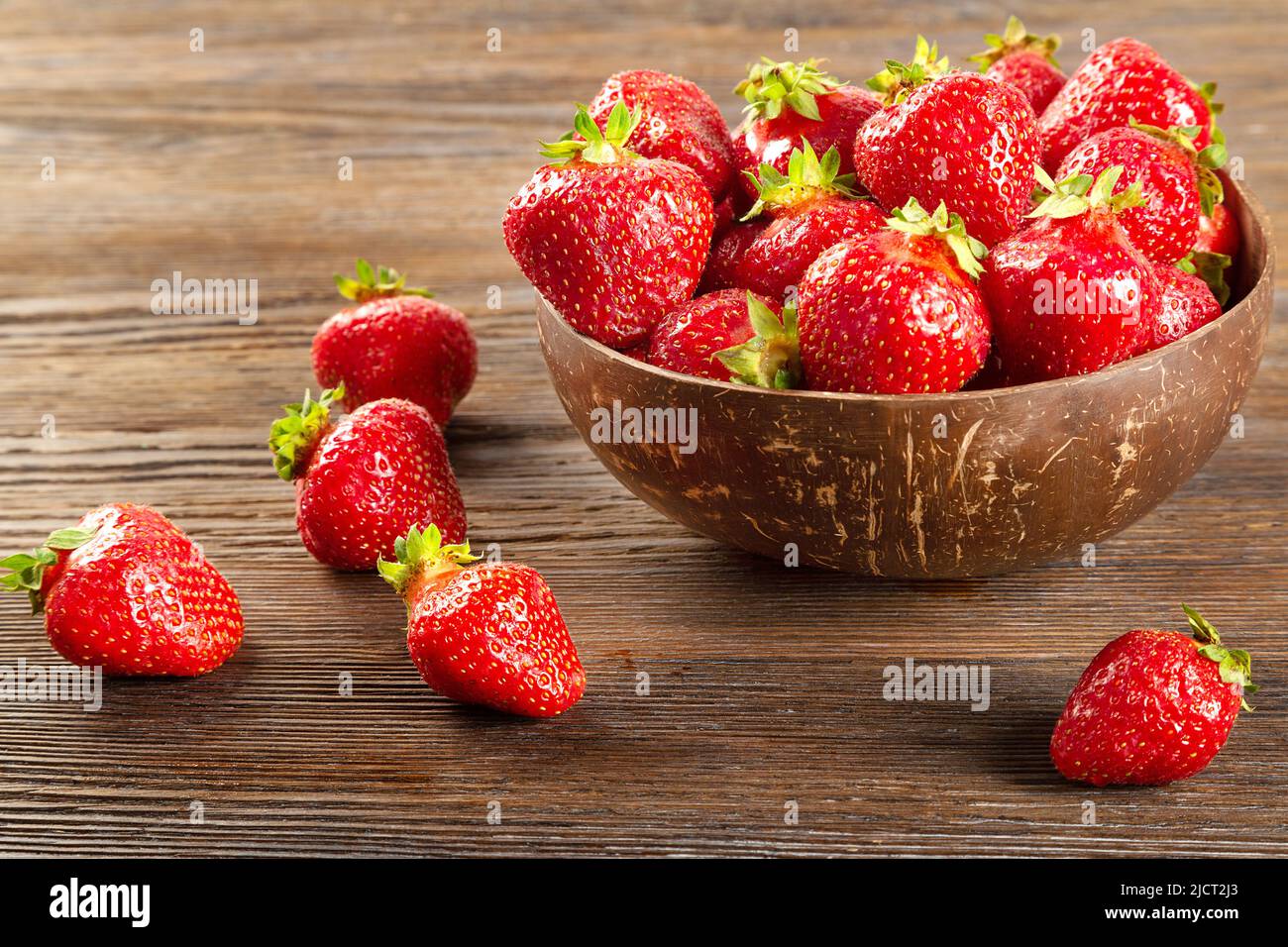 Fresh juicy ripe red strawberry in a coconut plate on a brown wooden ...