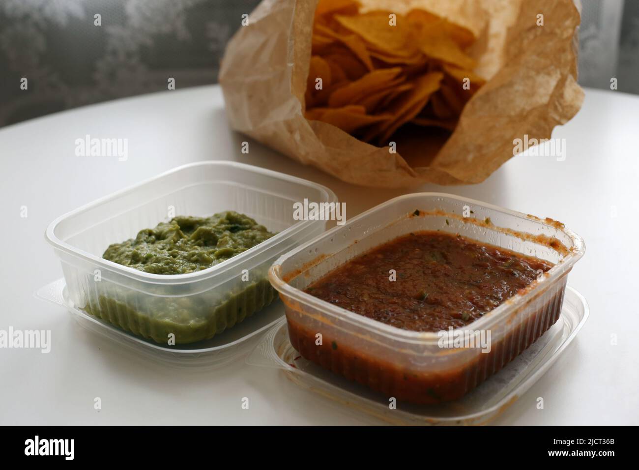 Mexican takeaway appetizer food on a table. There is a box of salsa, a ...