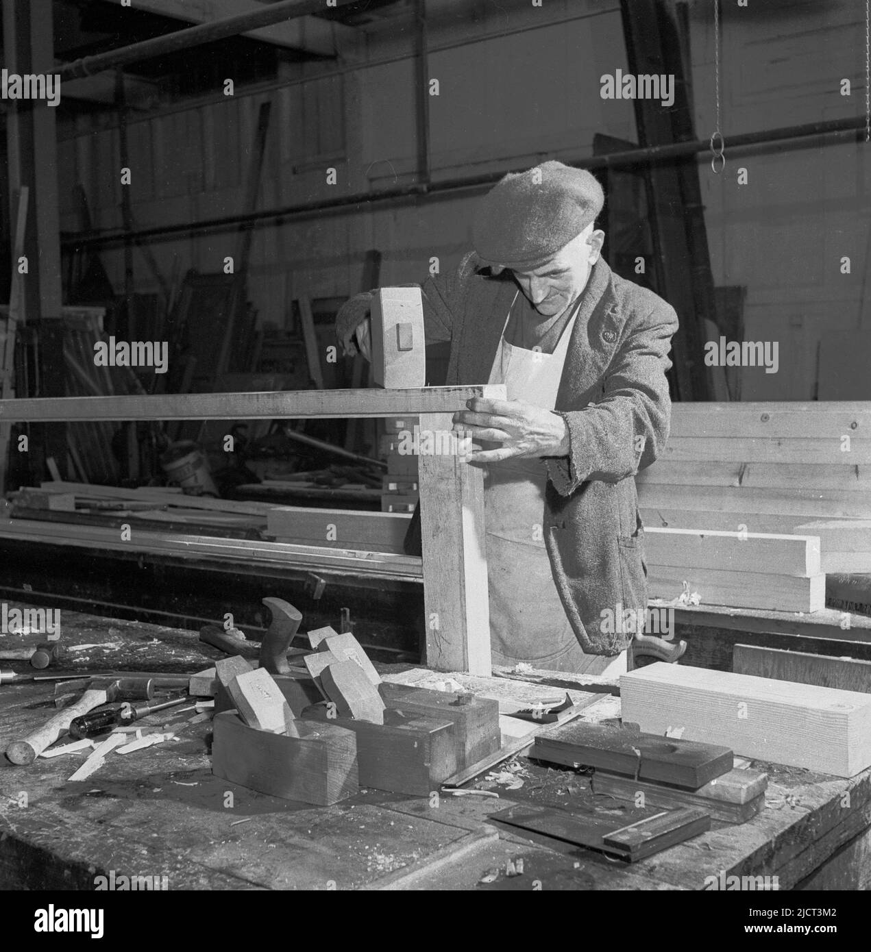 1950s, historical, a carpenter in a jacket and cloth cap, standing at a ...