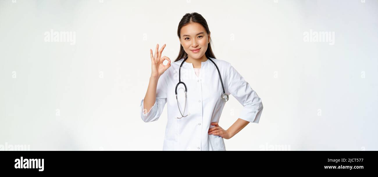 Very good. Smiling confident asian female doctor, showing okay, ok sign ...