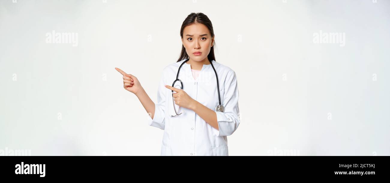 Sad and concerned female doctor, pointing fingers left, showing smth ...
