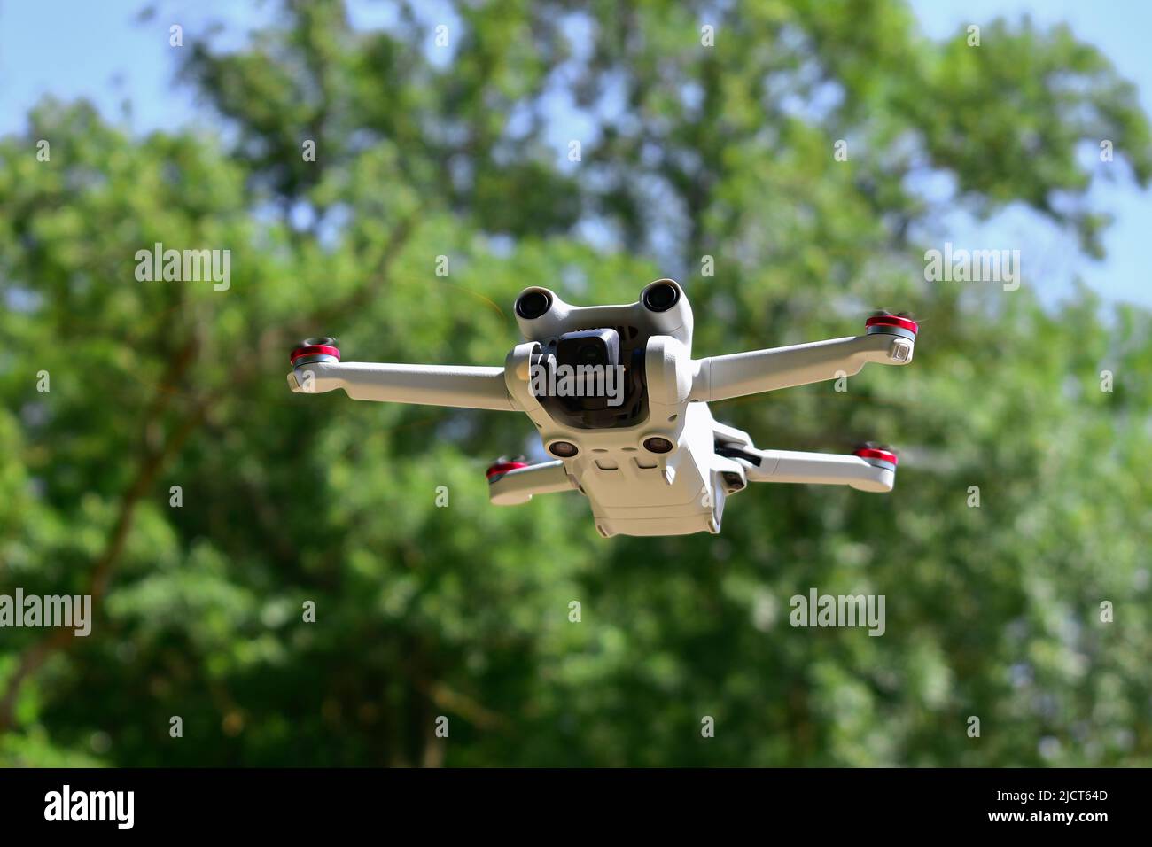 Small white mini drone flying up in front of forest, shallow depth of ...