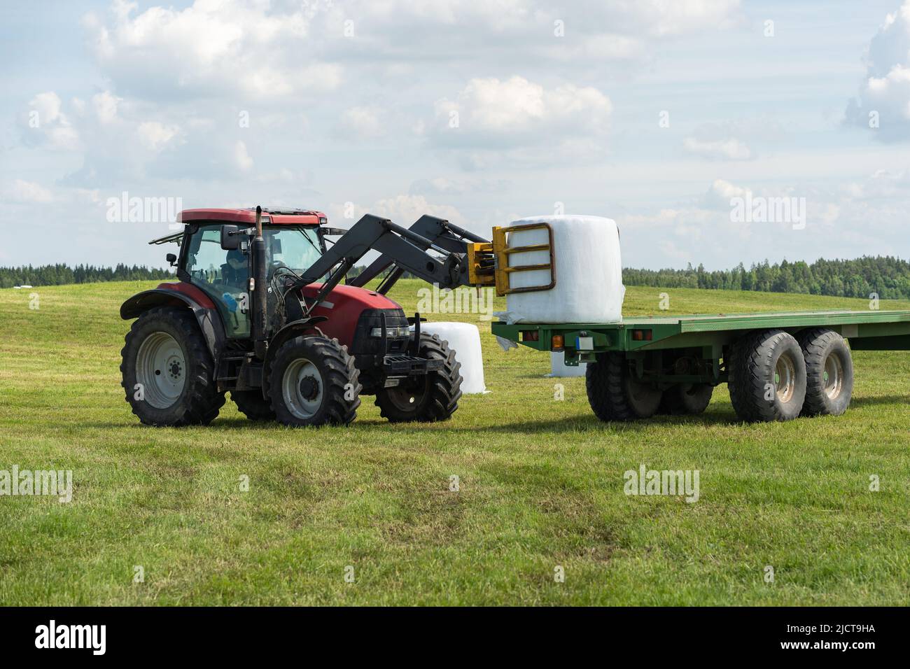 Lithuanian farmer using tractor with frontal handler to load hay bales ...