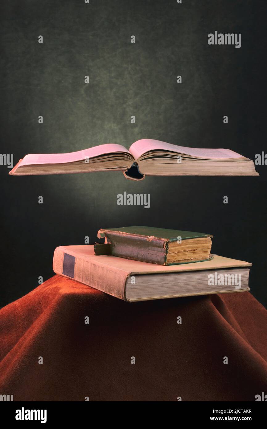 Still life with old books on the table and one open book floating in ...