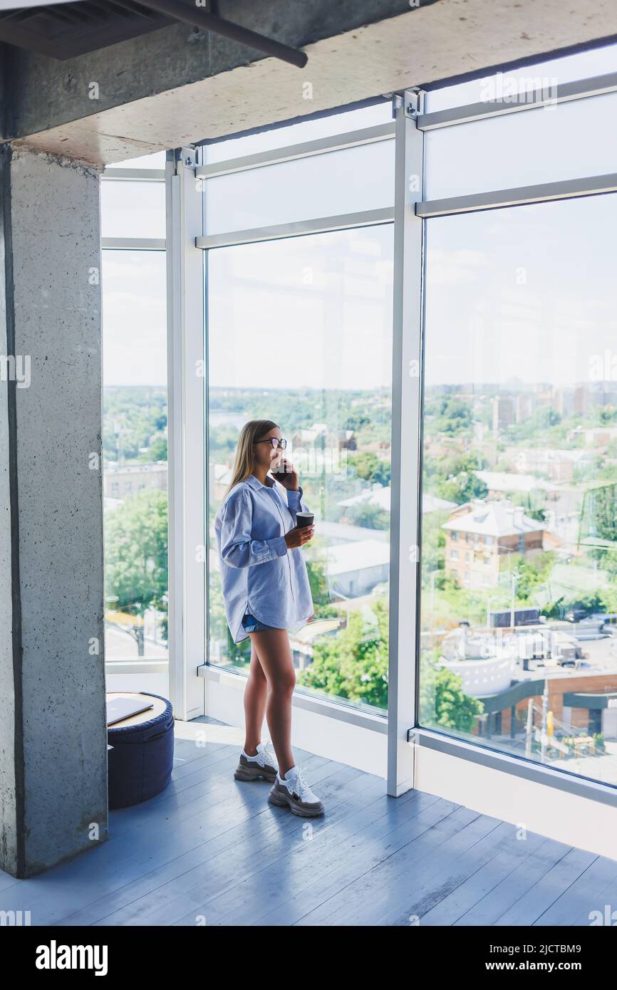Happy woman drinks coffee and looks out the window in a cafe. A young ...